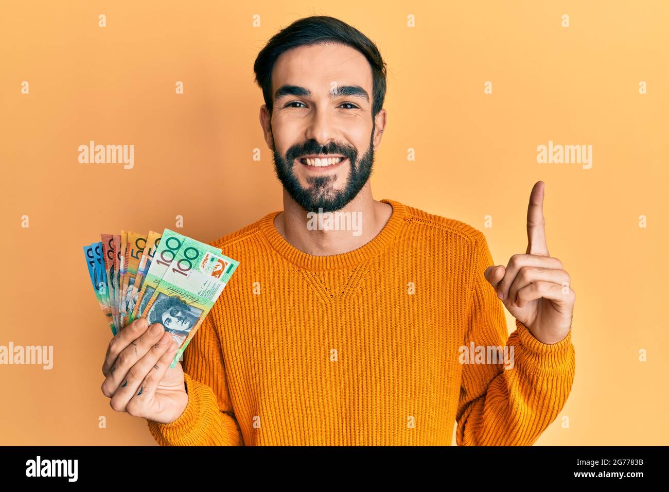 Young hispanic man holding australian dollars smiling with an idea or ...