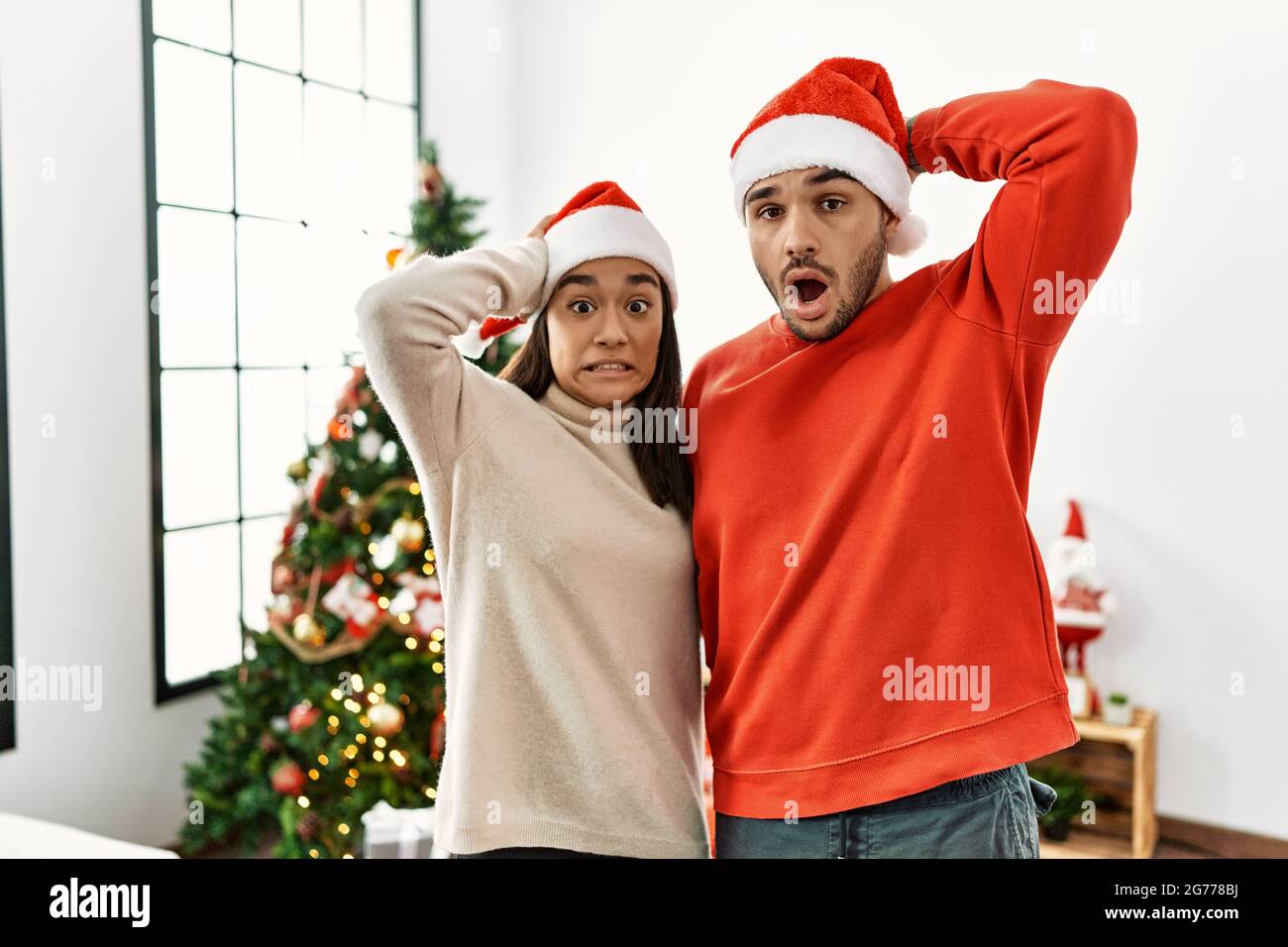 Young hispanic couple standing by christmas tree crazy and scared with ...