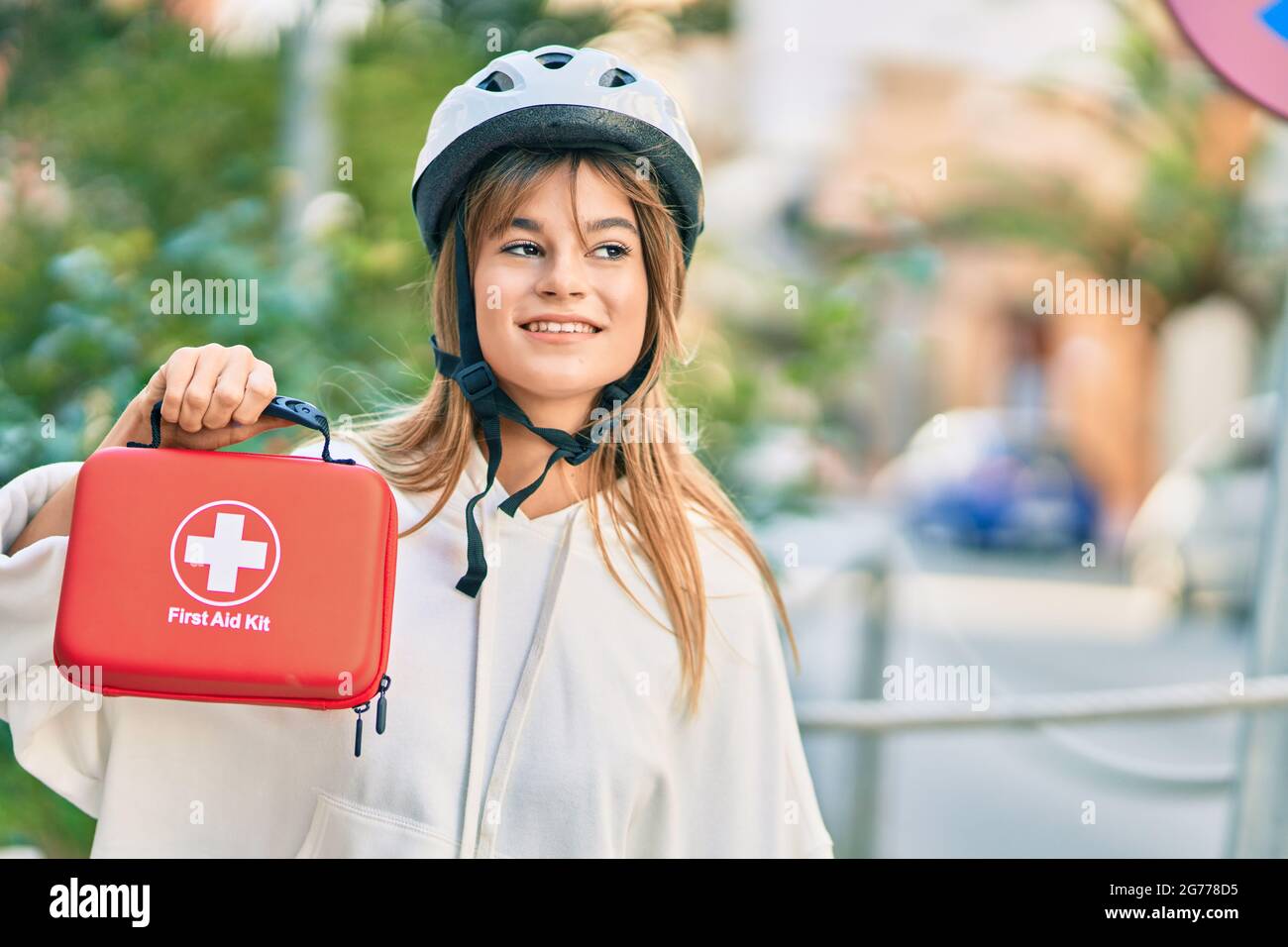 Caucasian sporty teenager girl wearing bike helmet holding first aid ...