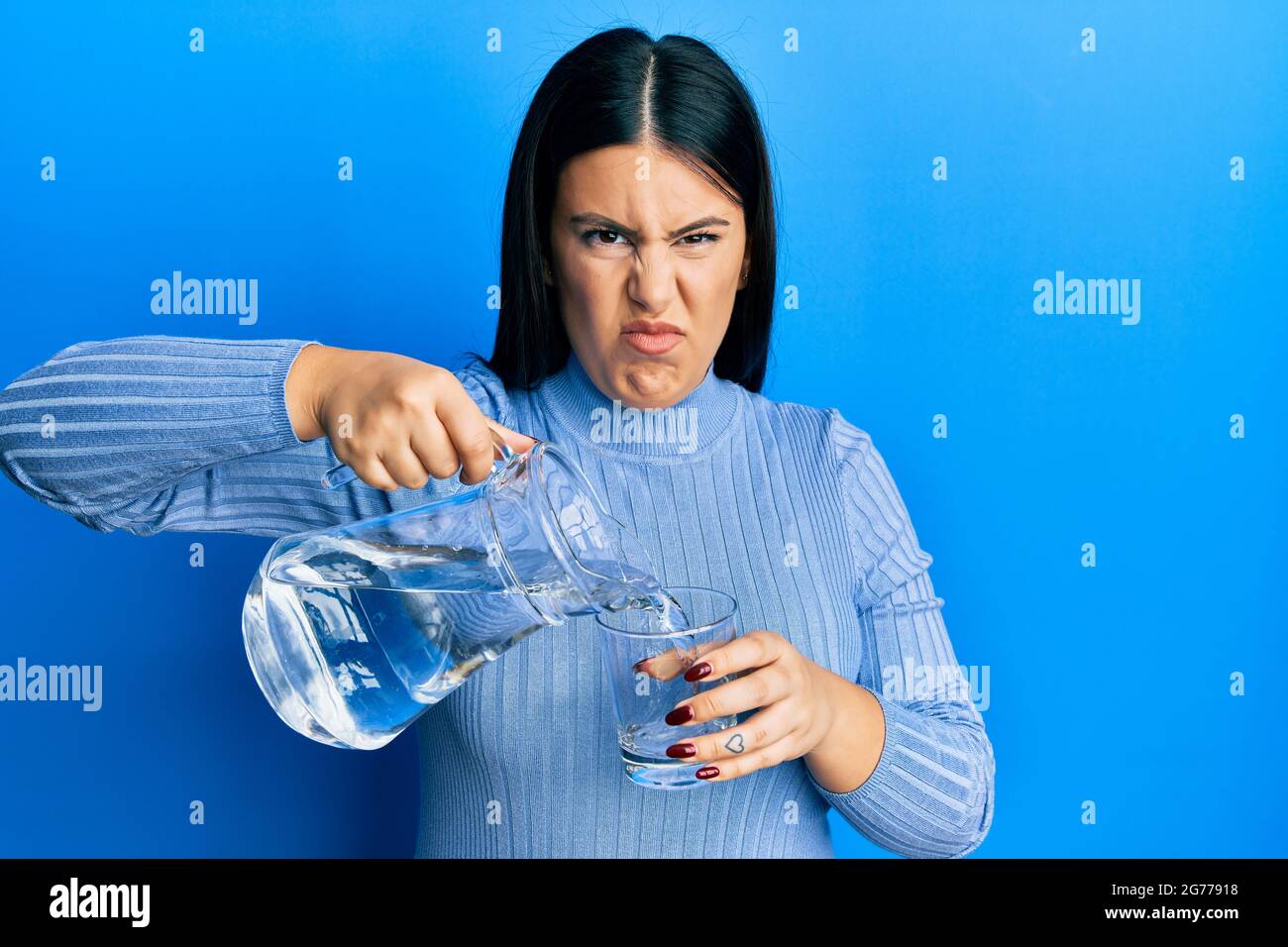 Beautiful brunette woman pouring water in glass skeptic and nervous ...