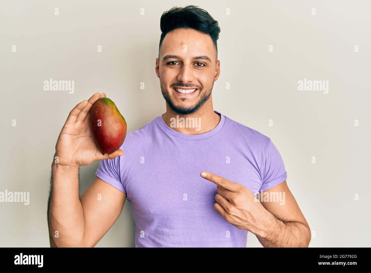 Young arab man holding mango smiling happy pointing with hand and ...