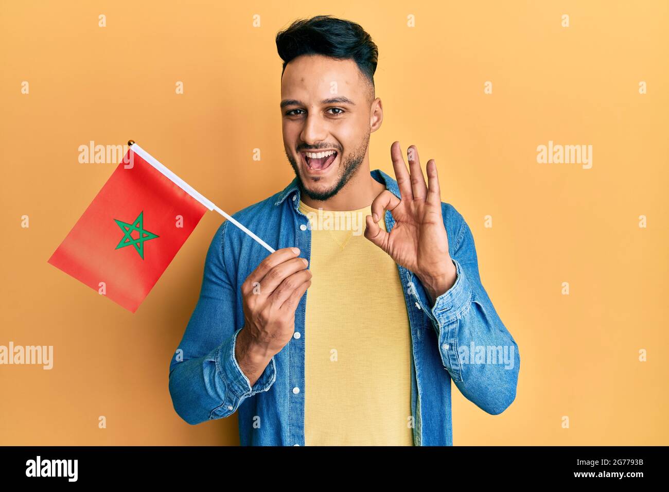 Young arab man holding morocco flag doing ok sign with fingers, smiling ...