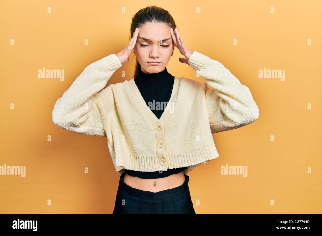 Young brunette girl wearing casual yellow jacket with hand on head ...