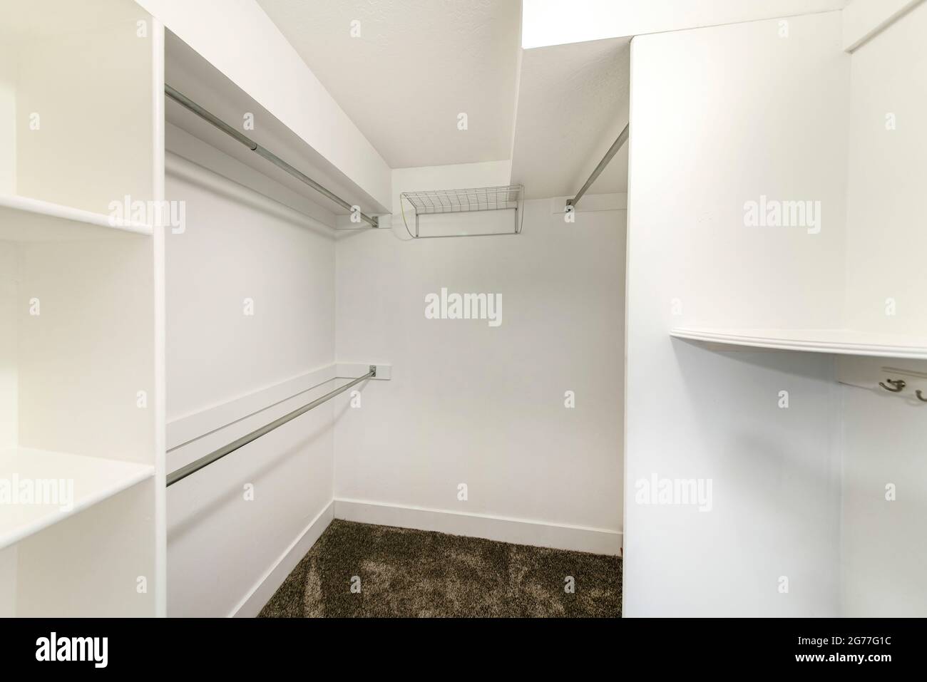 Interior of a plain white walk in closet with shelvings and carpeted ...