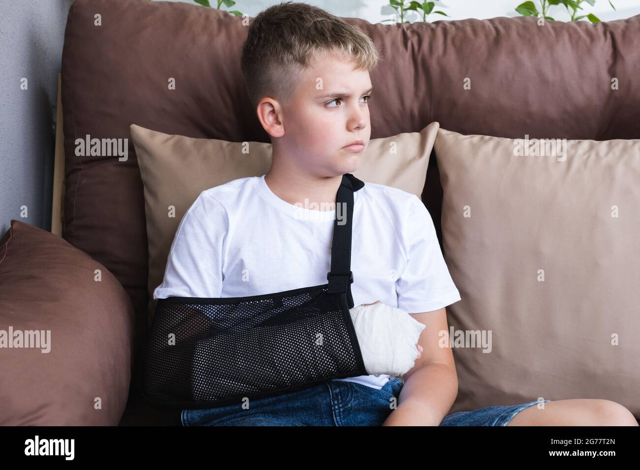 Sad child with a broken arm in home environment . Cast on hand of ...