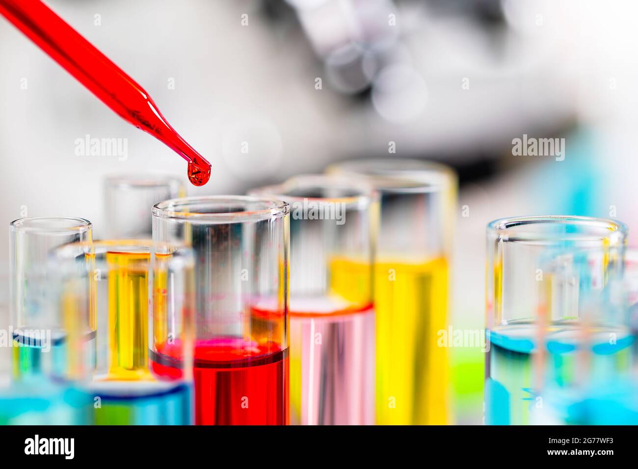 Red water drop in test tube dropper over colorful liquid in tube glass ...
