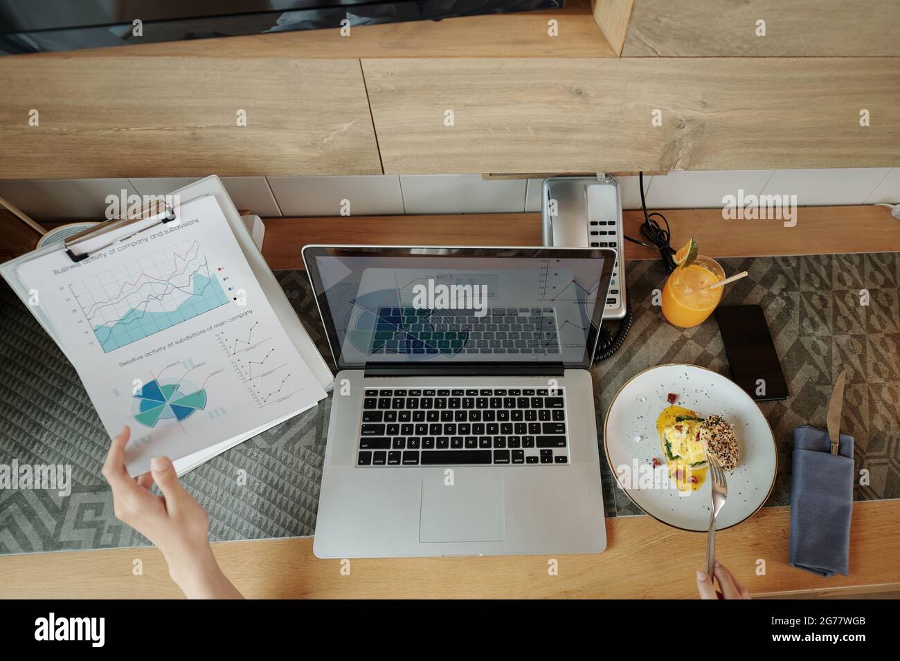 Female entrepreneur analyzing report with financial data and eating ...