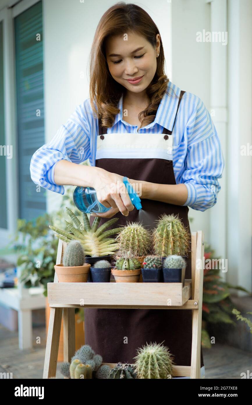 Cute Asian housewife wearing apron holding water sprayer and watering ...