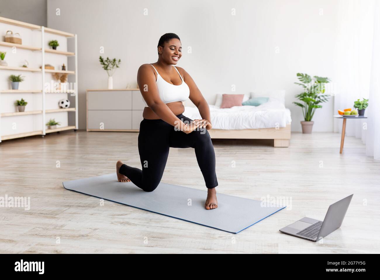 Full length of overweight black woman exercising to online sports video ...