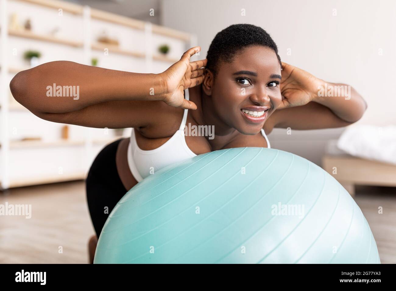 Cheerful plus size black woman doing exercises with fitness ball ...