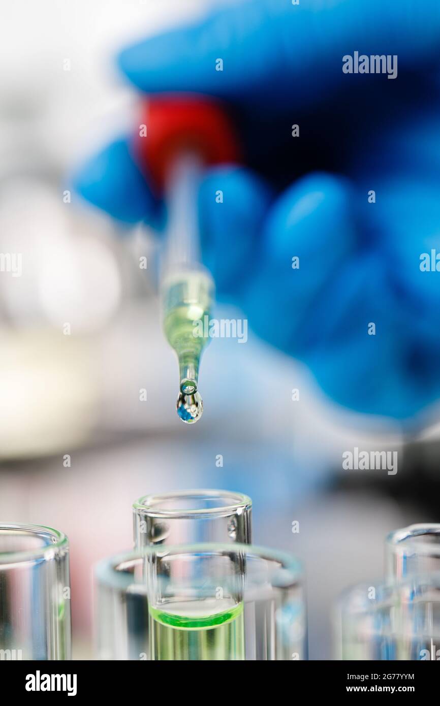 Hand wearing blue gloves holding droper and dropping water drop into ...