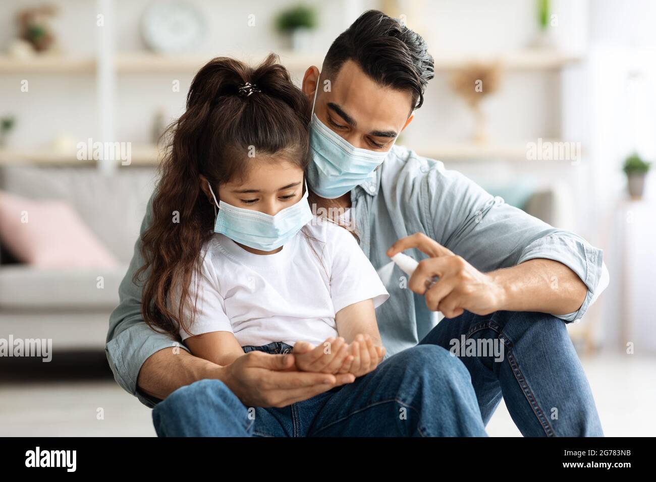 Middle-eastern father and daughter in face masks using disinfectant ...