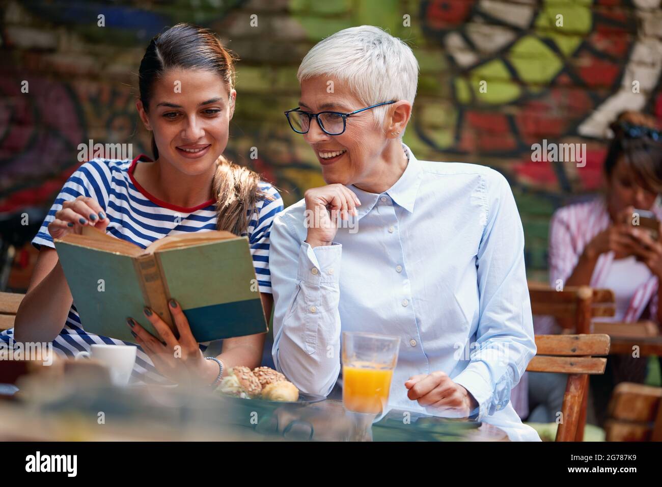 young adult woman reading a book together with elderly caucasian female ...