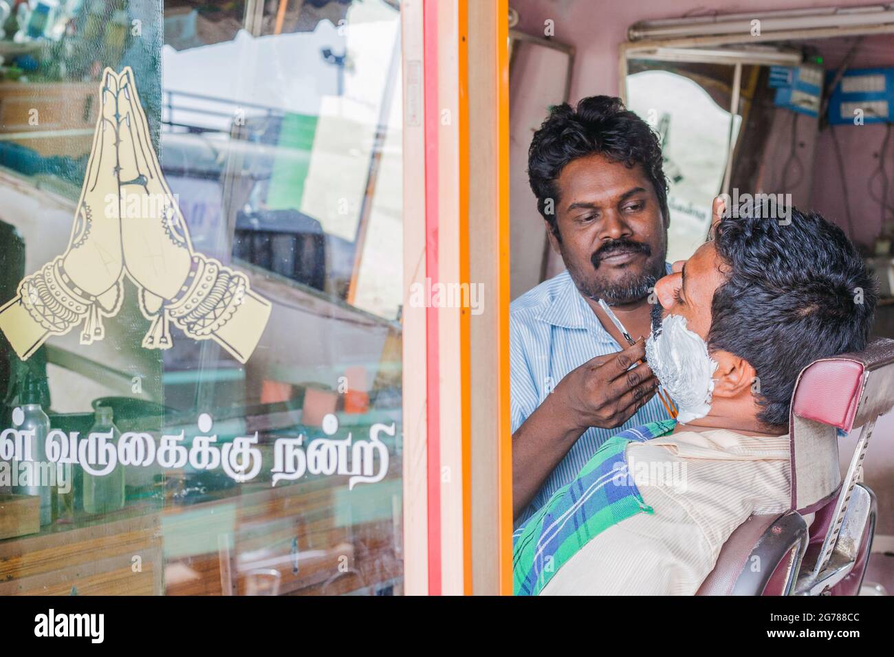 Indian barber brandishing cut throat razor gives a customer a shave ...