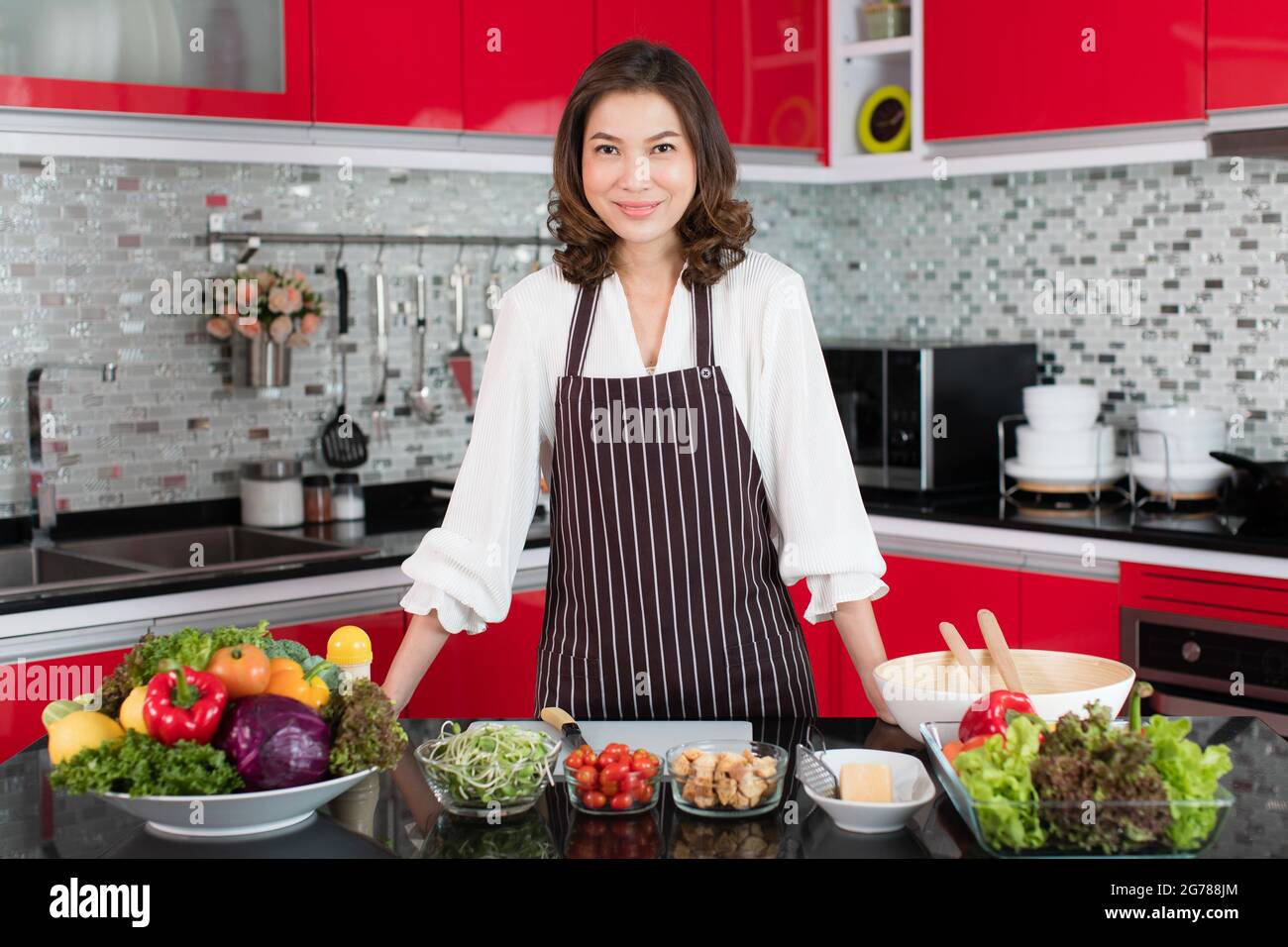 Asian cute middle-age woman in an apron standing on modern red tone new ...