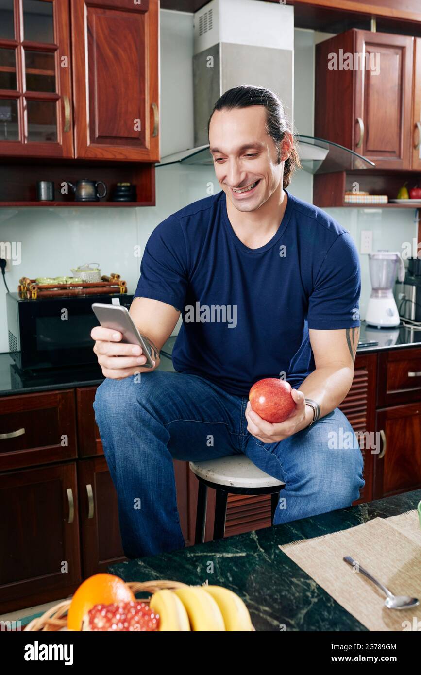 Cheerful man eating red apple and looking at funny memes on social ...