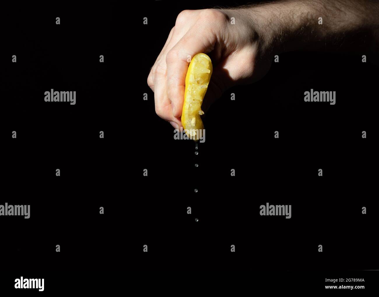 lemon with leaking juice squeezed in hand of man on black background ...