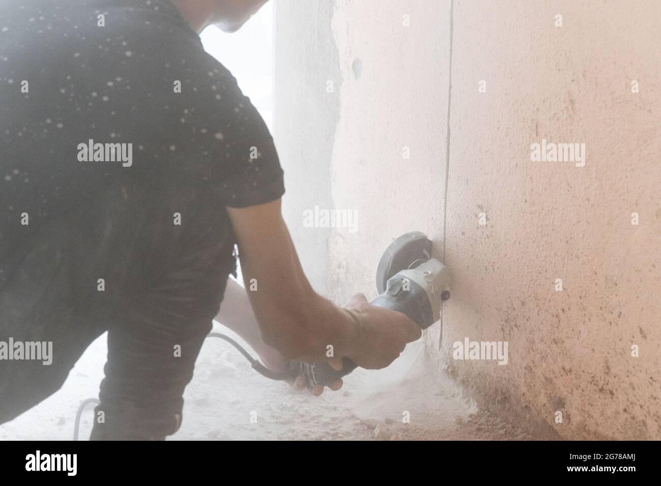 Worker cutting concrete wall with disc cutting tool, resulting dusk ...