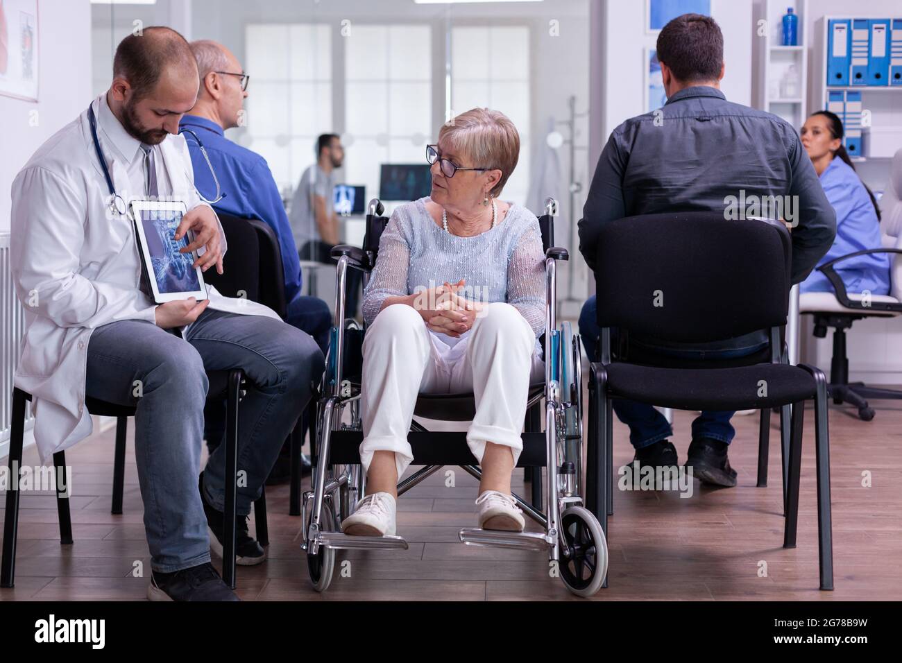 Doctor man sitting in waiting hospital area with senior disability ...
