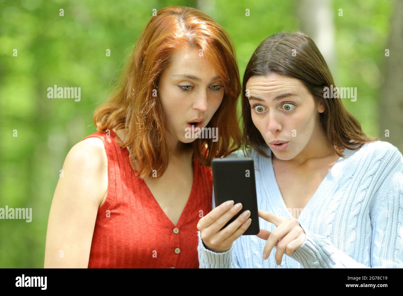 Two amazed women friends checking surprising smart phone content in a ...