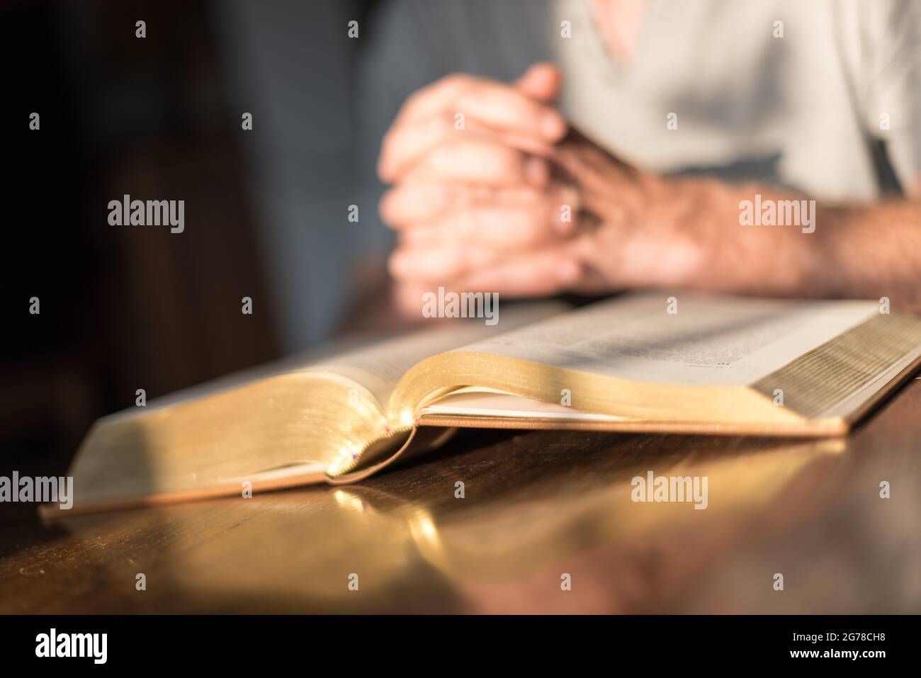 Man praying hands on a Bible in dim light Stock Photo - Alamy