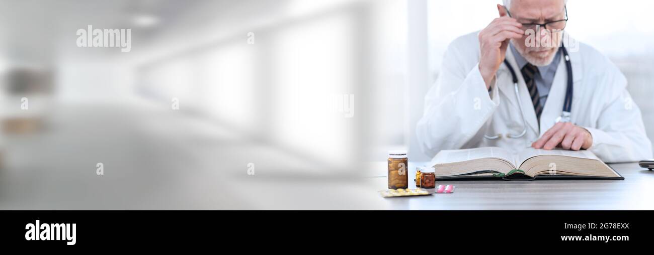 Senior doctor reading a textbook in medical office; panoramic banner ...