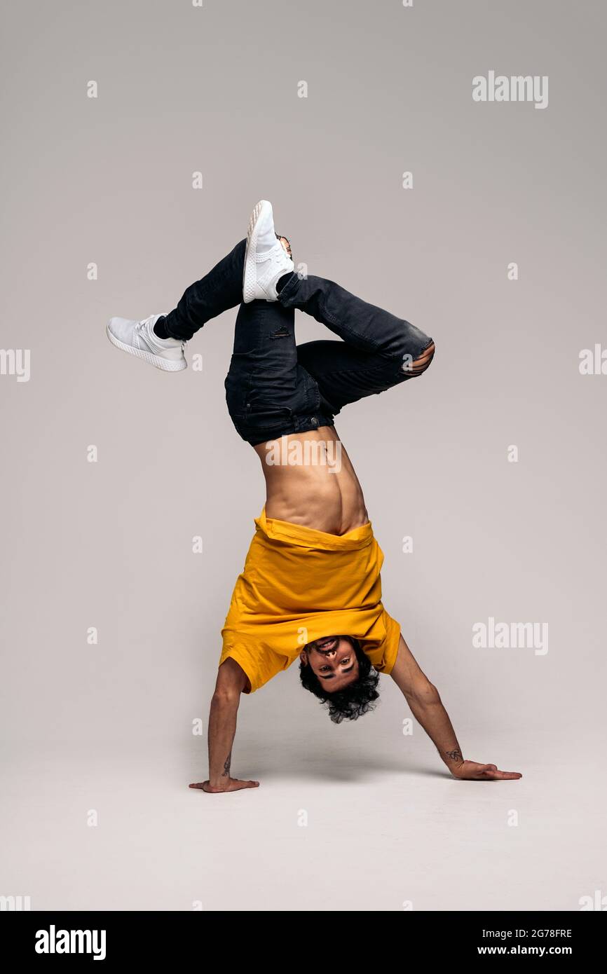 Energetic male dancer wearing casual clothes doing handstand in studio ...