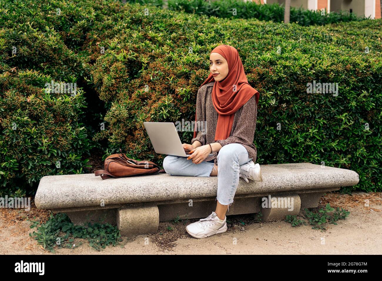 Young muslim woman wearing hijab sitting in the park and using her ...