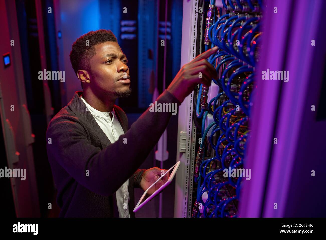 Concentrated young Black IT engineer standing with tablet in data ...