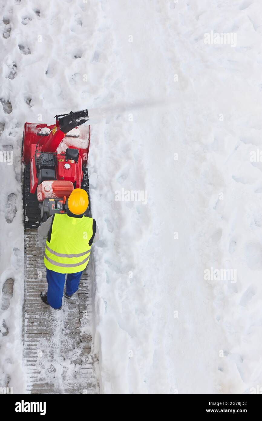 Worker cleaning snow on the sidewalk with a snowblower. Maintenance ...