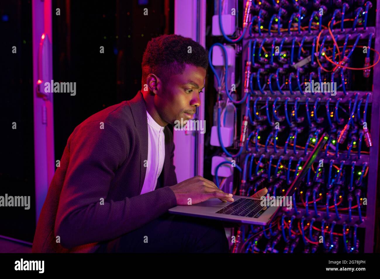 Concentrated young African-American programmer crouching near open ...