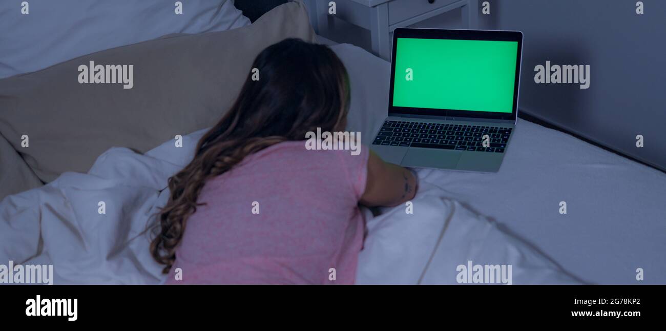 Young woman lies on the bed with her laptop - green screen display ...