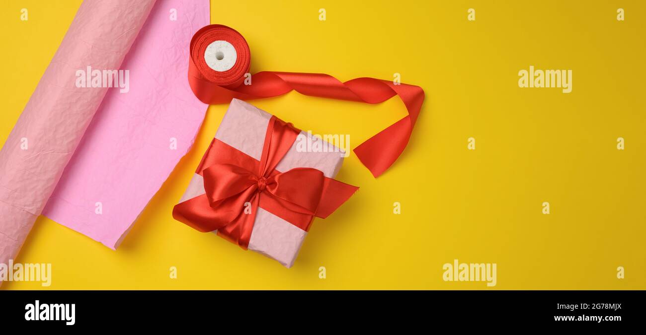 pink gift box wrapped in red silk ribbon on yellow background, copy ...