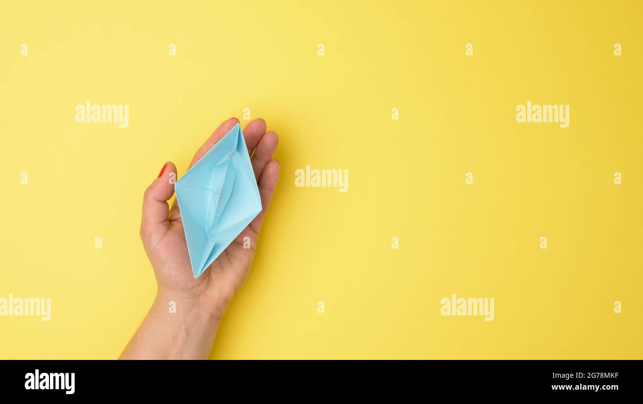female hand hold a blue paper boat on a yellow background. Mentoring ...