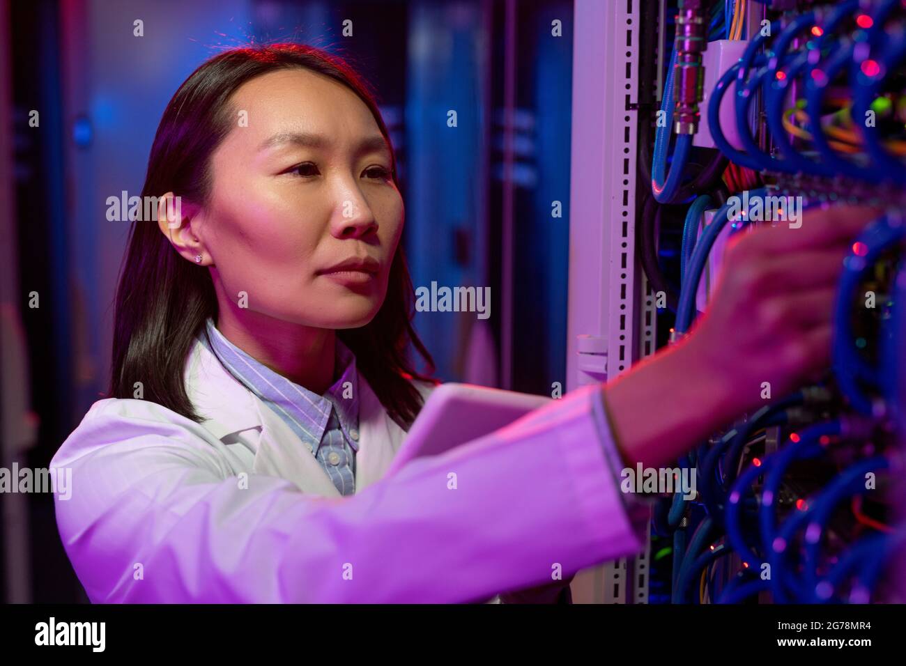 Busy young Asian female network specialist standing at cabinet in dark ...