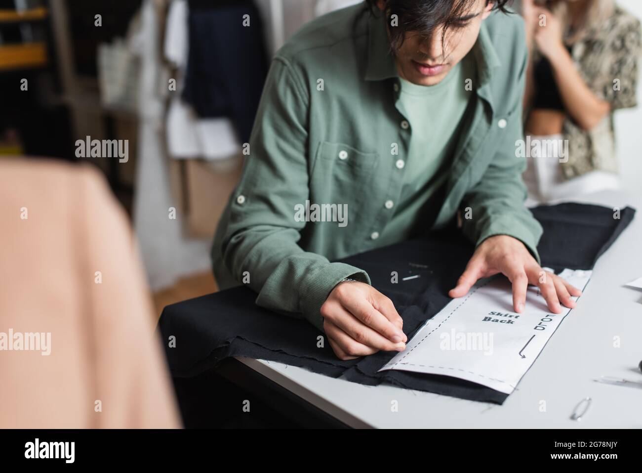 young fashion designer working with sewing pattern and fabric in tailor ...