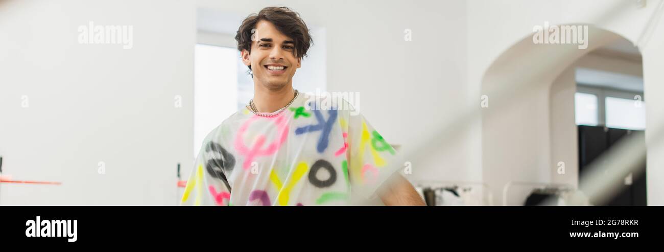 happy and trendy designer smiling at camera in fashion workshop, banner ...