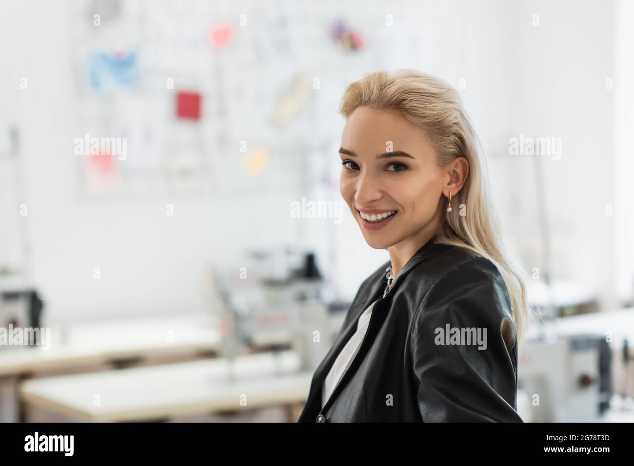 joyful, trendy fashion designer smiling at camera in tailor shop Stock ...