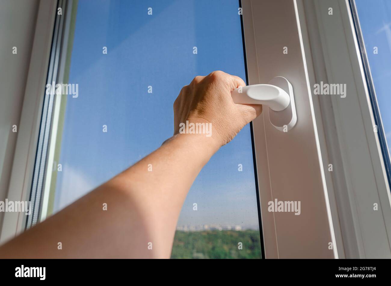 Woman's hand opens the handle of a plastic window against a blue sky ...
