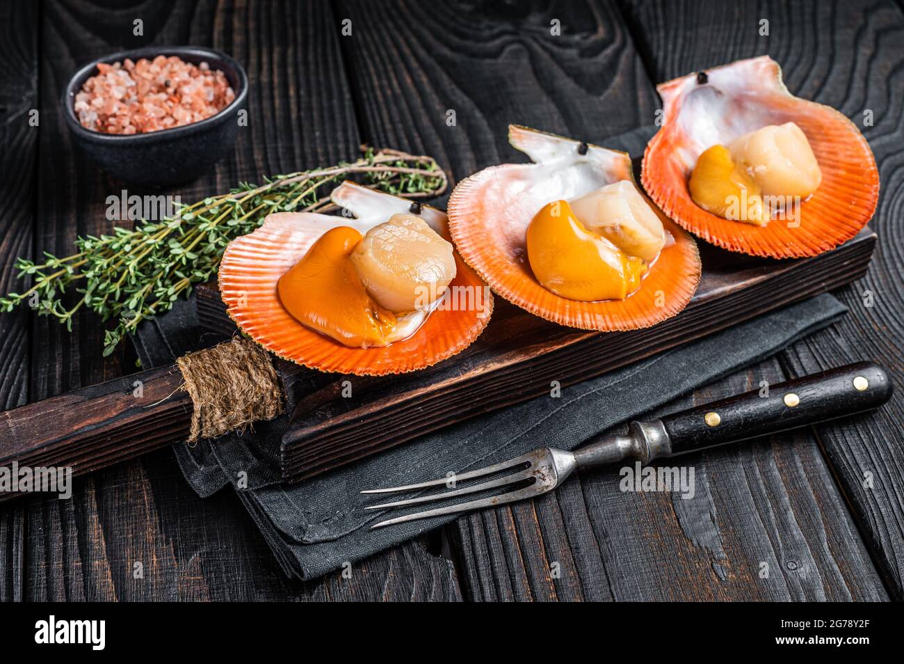 Scallops raw Shellfish on a wooden board with herbs. Black wooden ...