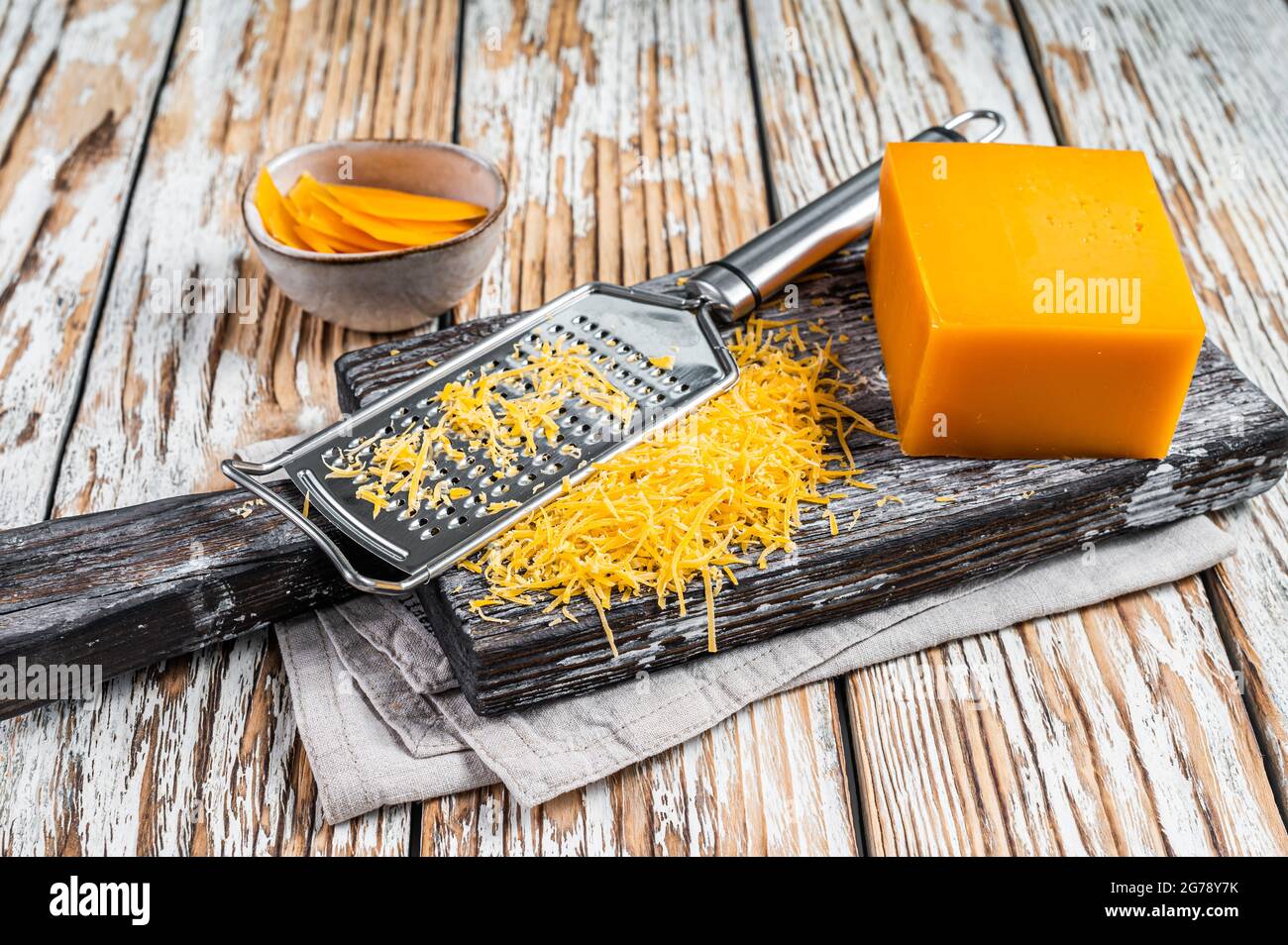 Grated Cheddar Cheese on a wooden cutting board. White wooden ...