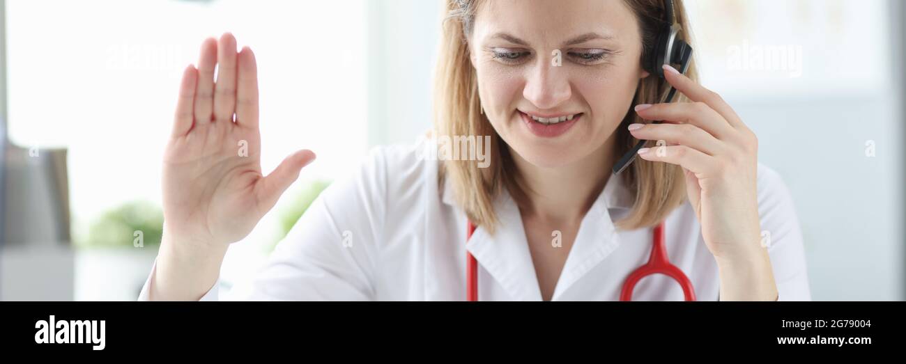 Woman doctor in headphones waving hand at laptop screen. Remote patient ...