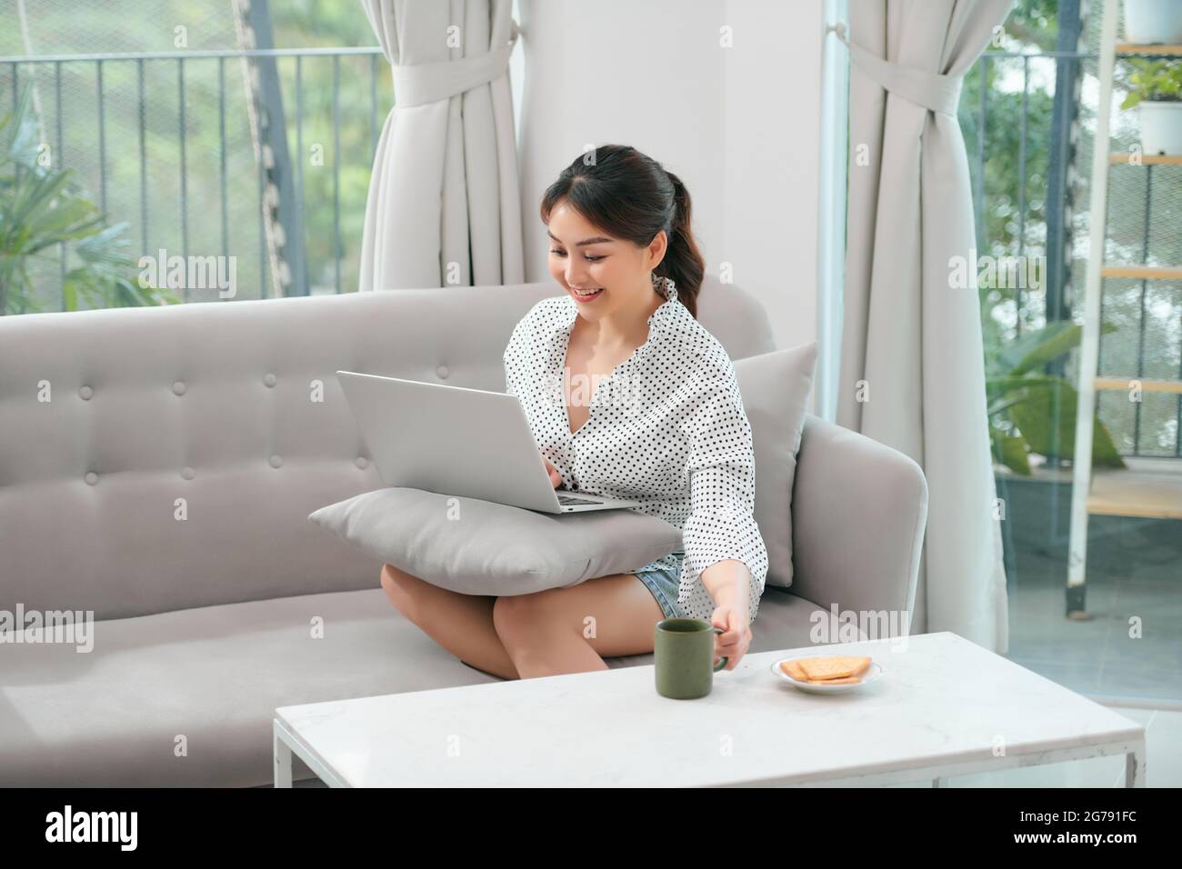 Image of cheerful asian woman using laptop while sitting on couch in ...