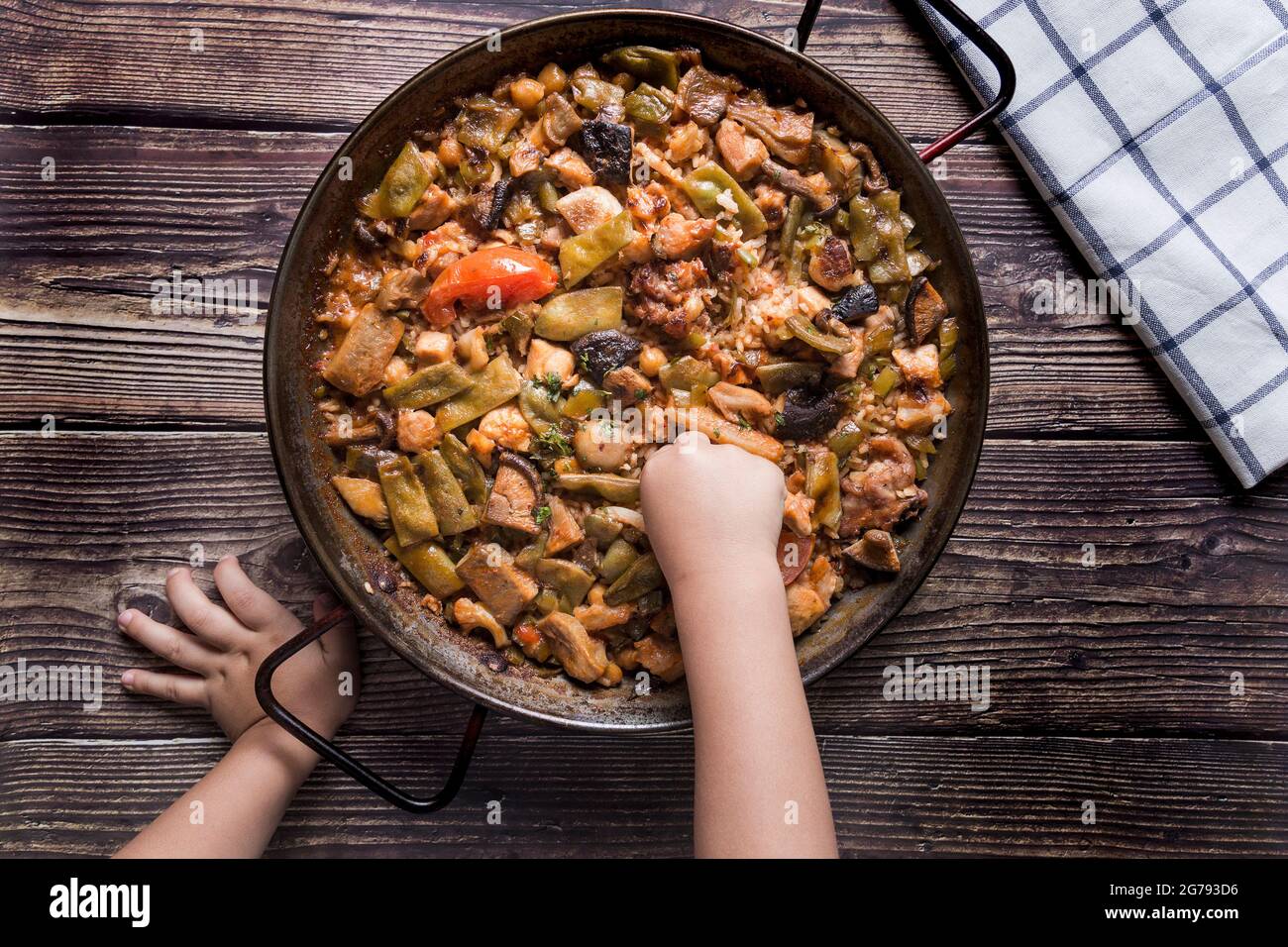 Child's hand trying a paella. Wooden table with a traditional homemade ...