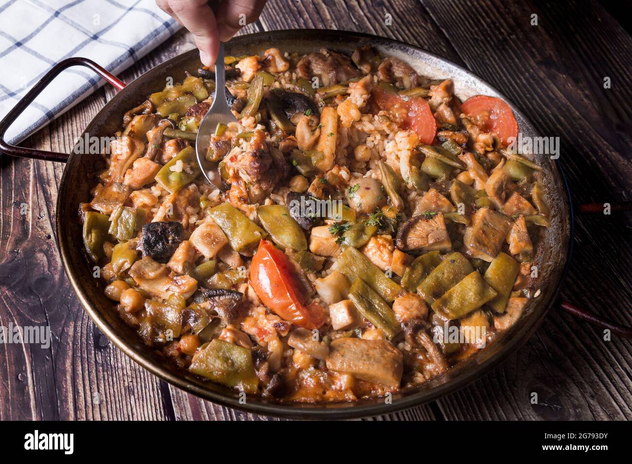 A man's hand, eating a vegetable paella with a spoon. Tasting a ...