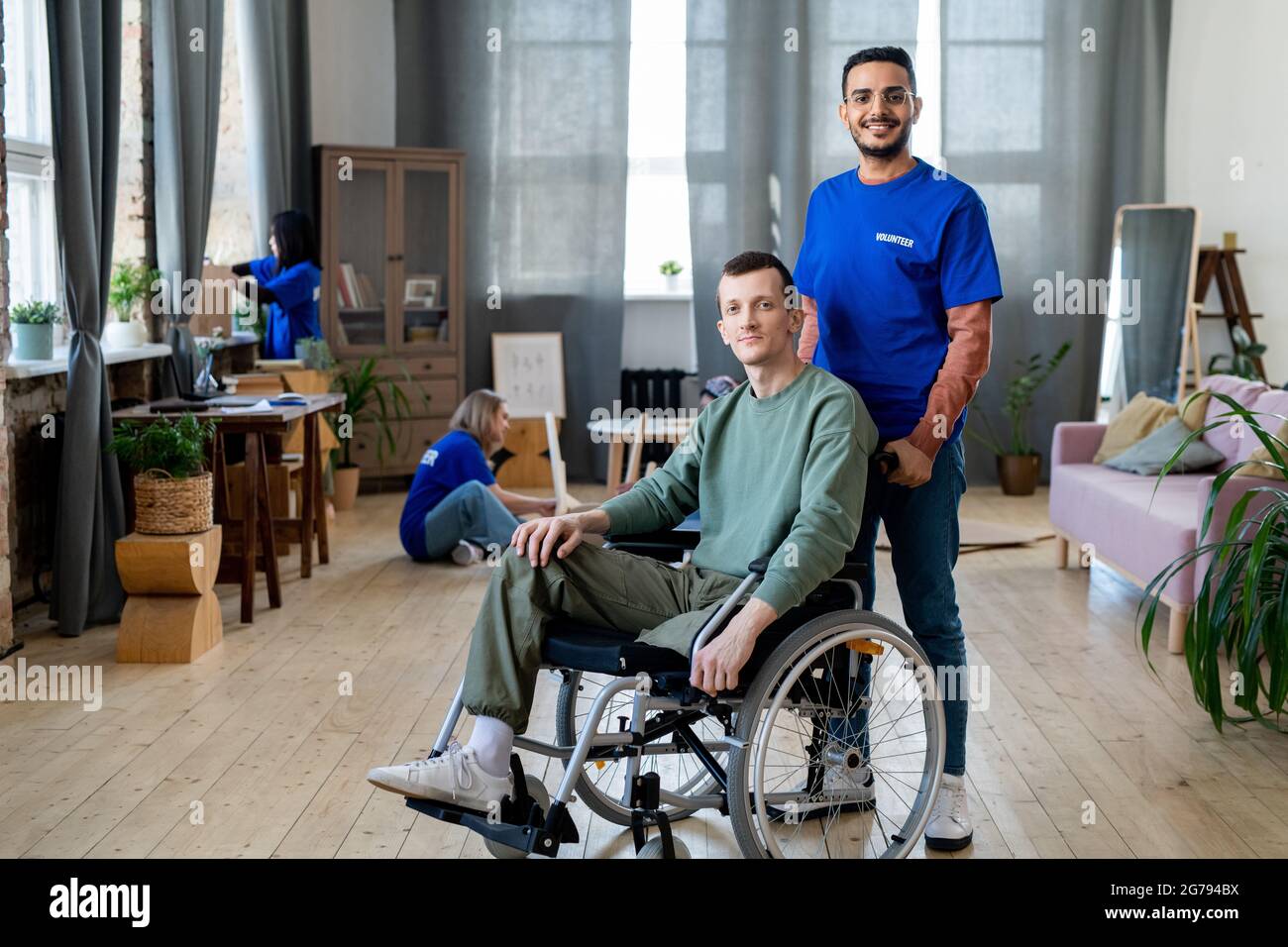 Happy young male volunteer taking care of disabled guy in wheelchair ...