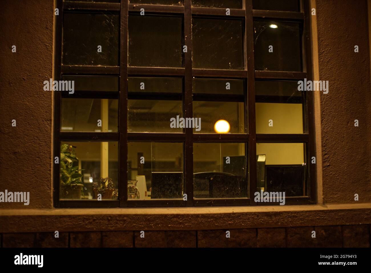 A dirty office building window at night with lamp post reflections ...