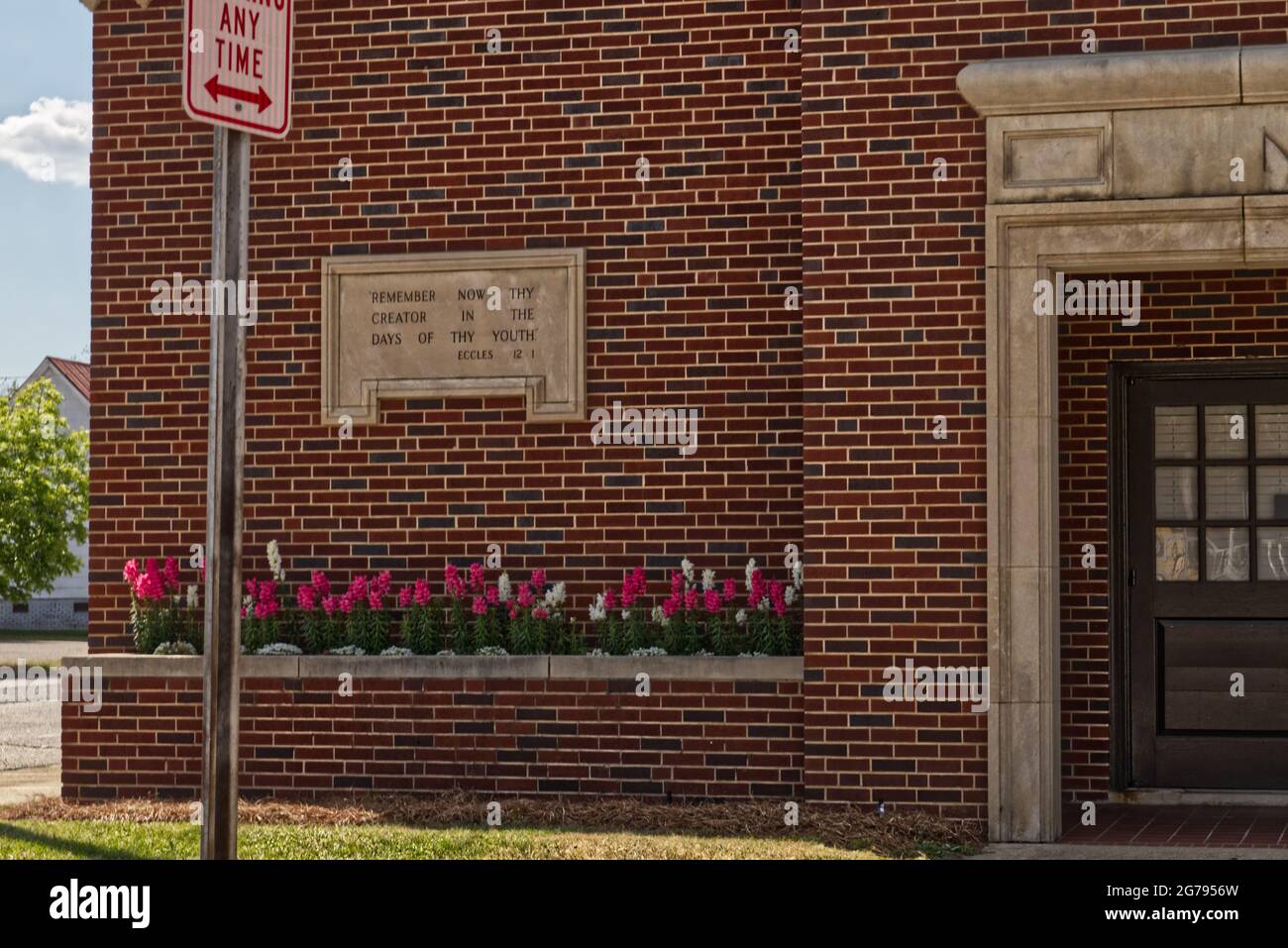 A scripture engraved in stone on a brick wall with a flower bed ...