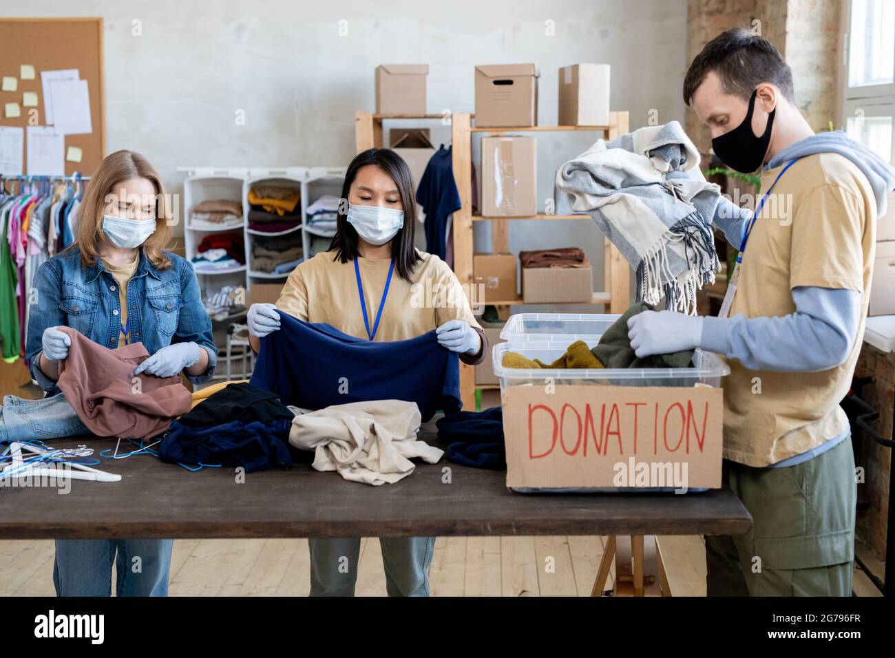 Three volunteers in masks and gloves sorting donation clothes Stock ... Three volunteers in masks and gloves sorting donation clothes Stock ...