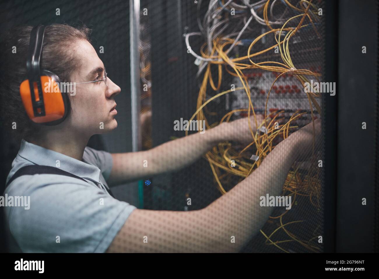Side view of young network engineer connecting cables in server room ...